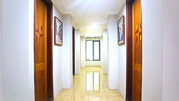Um corredor com portas de madeira e quadros nas paredes, que dá acesso a um quarto com janela.