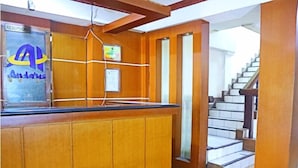 Uma área de recepção com balcão de madeira, mesa de atendimento e escada para um andar superior.