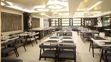 Uma sala de jantar espaçosa com várias mesas e cadeiras, um design de teto moderno e um logotipo no canto superior direito.