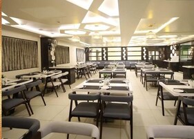 Uma sala de jantar espaçosa com várias mesas e cadeiras, um design de teto moderno e um logotipo no canto superior direito.