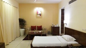 Quarto de hotel com duas camas, um sofá, uma mesinha, uma planta e um ventilador de teto.