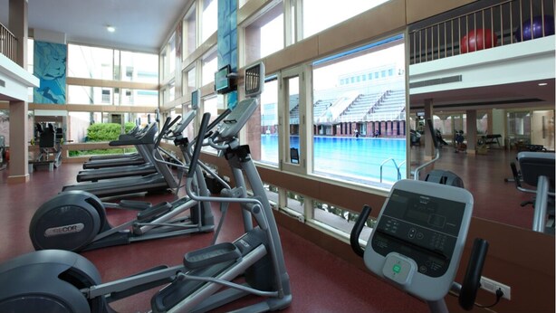 Uma academia com esteiras, aparelhos de musculação e uma grande janela com vista para a área da piscina.