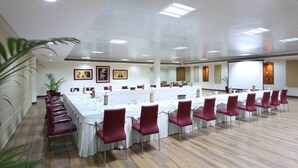 Uma sala de conferência com uma mesa comprida, cadeiras vermelhas e quadros nas paredes.