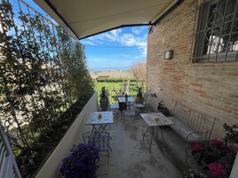 Um alpendre coberto com mesas e cadeiras, uma parede de tijolos e vista para o campo.
