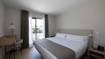Quarto de hotel com uma cama grande, uma escrivaninha, uma cadeira, um abajur e vista para o exterior.