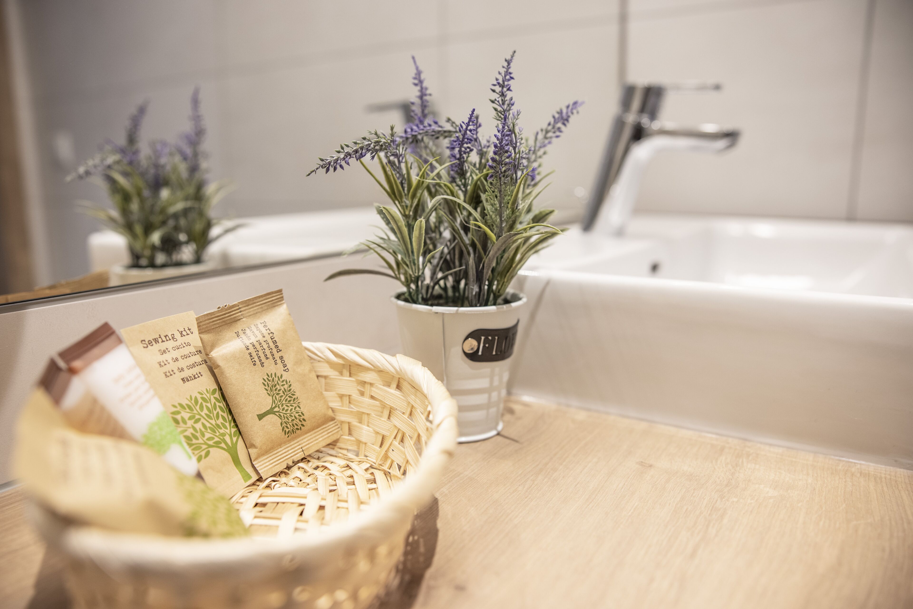 Casa de banho com uma banheira branca, uma planta de lavanda em vaso e uma cesta de vime com artigos de higiene pessoal.
