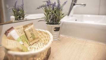 Casa de banho com uma banheira branca, uma planta de lavanda em vaso e uma cesta de vime com artigos de higiene pessoal.
