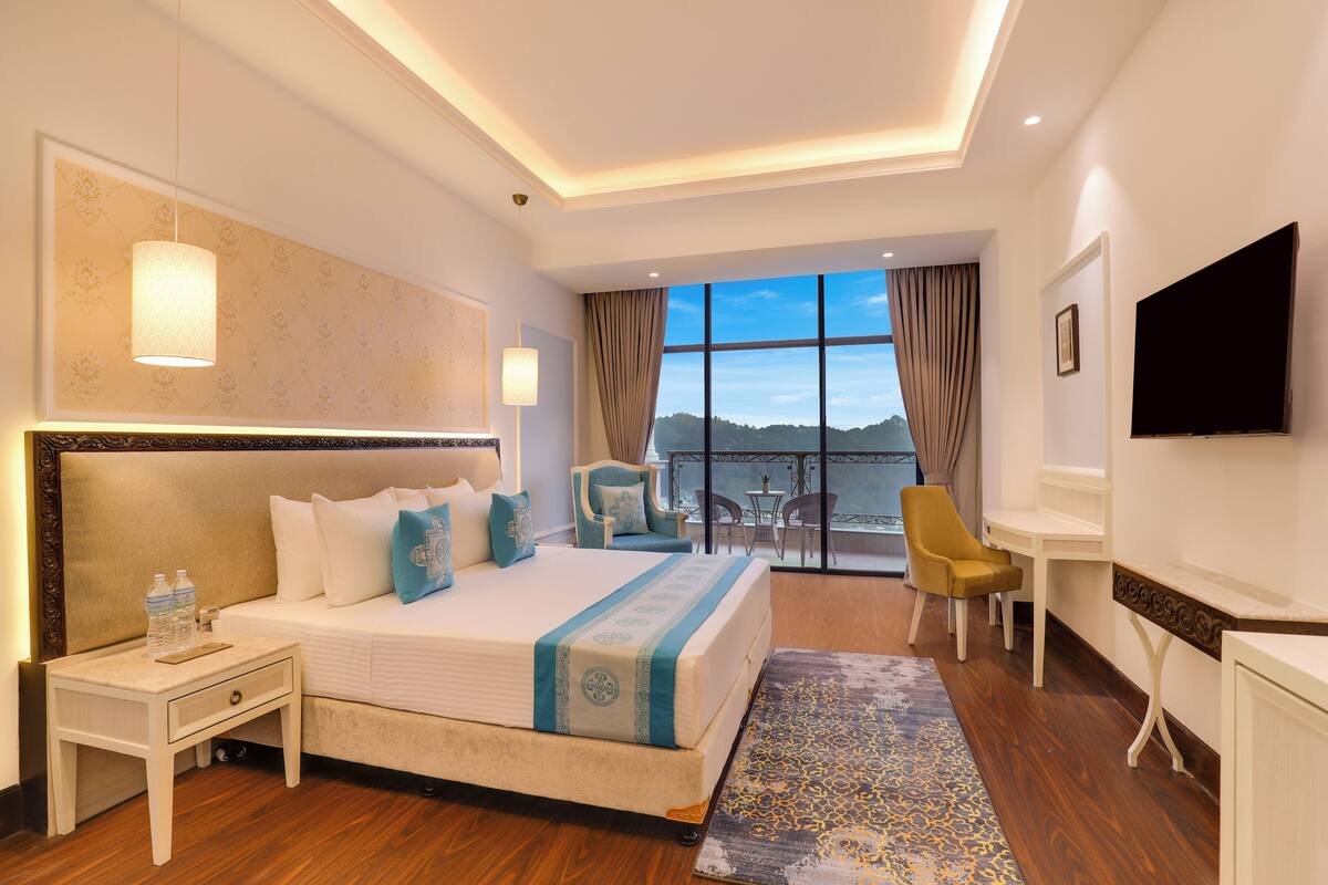 Quarto de hotel com uma cama grande, uma escrivaninha, uma cadeira, uma TV e uma varanda com vista.