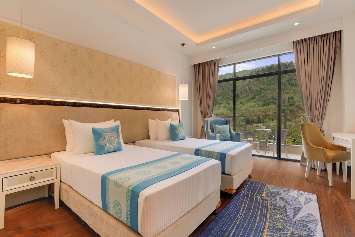 Quarto de hotel com duas camas, uma escrivaninha e vista para uma paisagem montanhosa.
