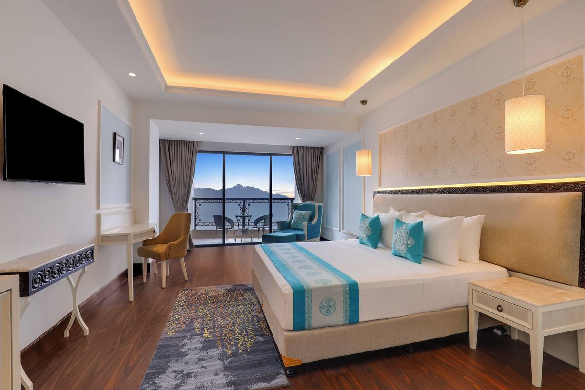 Quarto de hotel com uma cama grande, uma escrivaninha, uma cadeira, uma televisão e vista para as montanhas.