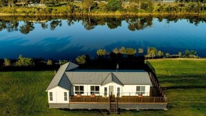 Uma casa com uma varanda grande, um alpendre coberto e vista para um lago.