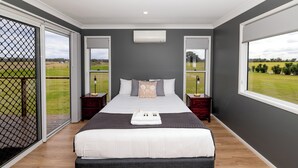Quarto com uma cama grande, duas mesas de cabeceira, uma janela com vista para um campo gramado e uma porta de vidro deslizante que dá para uma área externa.
