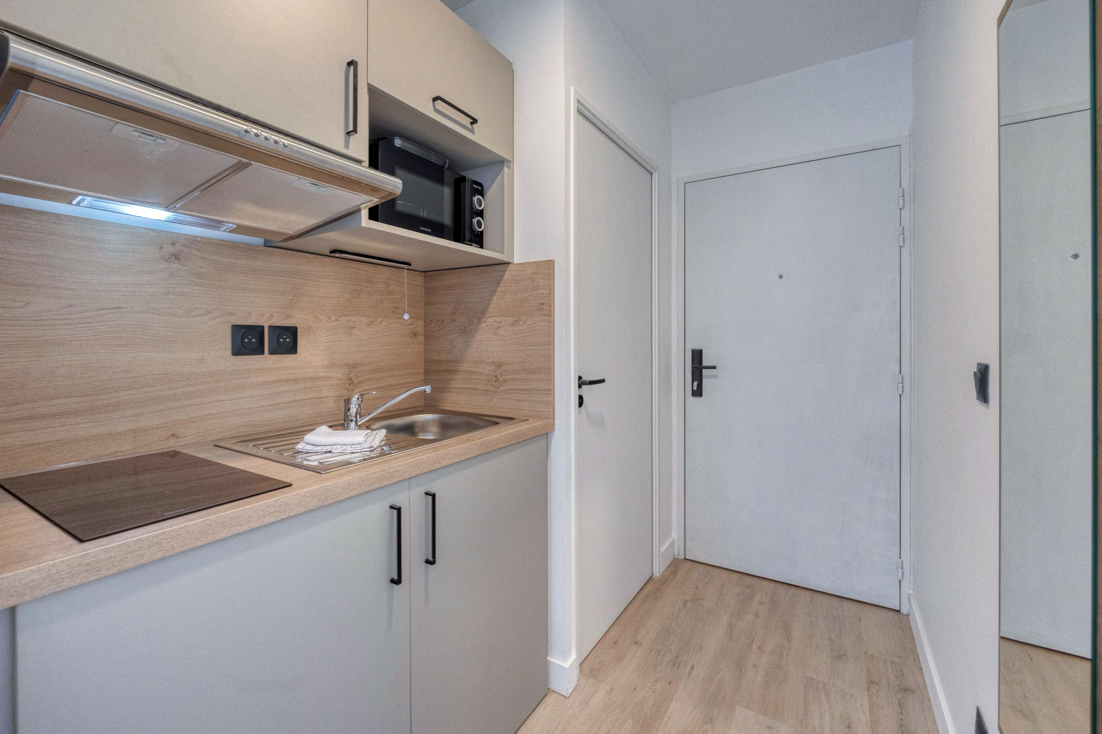 Cozinha compacta com micro-ondas embutido, pia e bancada de madeira.