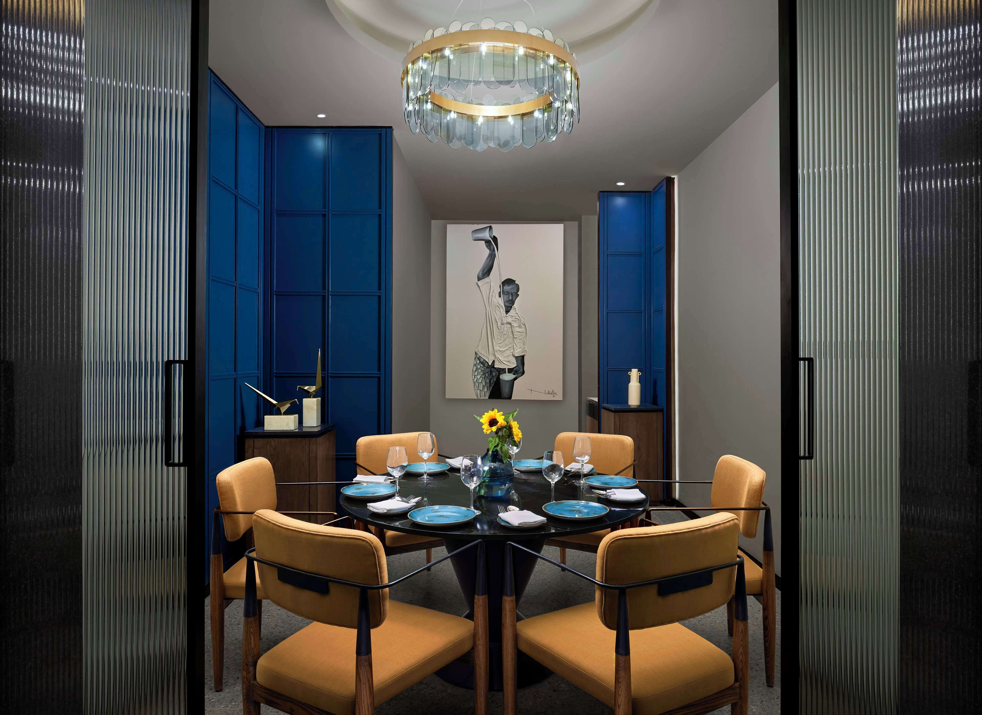 Uma sala de jantar moderna com uma mesa de vidro, painéis azuis e um lustre.