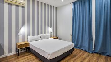 Quarto com cama, piso de madeira, parede listrada, ar condicionado, abajures e cortina azul.