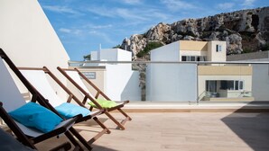 Terraço no topo com espreguiçadeiras e vista para um penhasco rochoso.