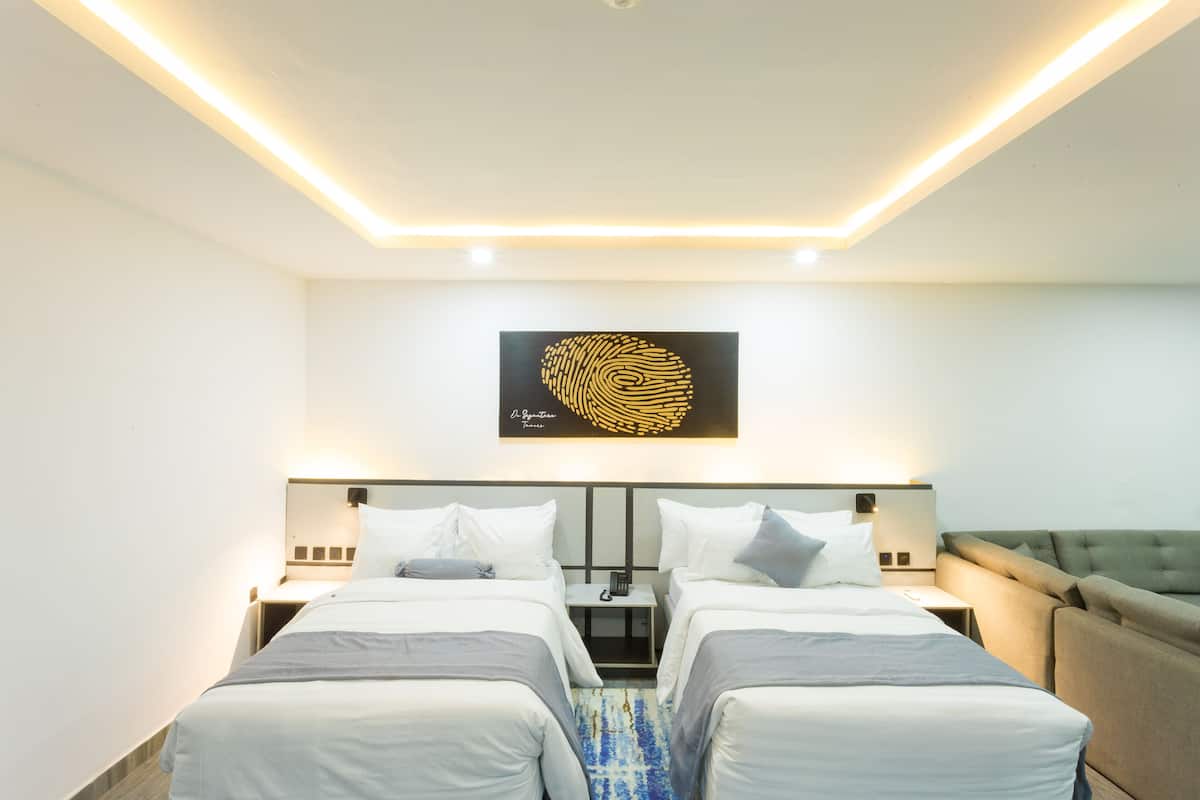 Quarto de hotel com duas camas, um sofá, uma obra de arte na parede e um candeeiro de teto.