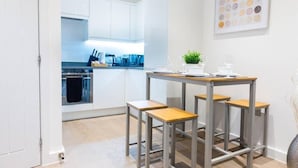 Uma cozinha compacta com armários brancos, forno embutido e área de jantar com mesa e banquetas.