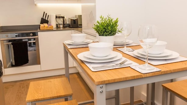 Cozinha moderna com armários brancos, bancada de madeira e mesa de jantar posta com pratos, tigelas e copos de vinho brancos.
