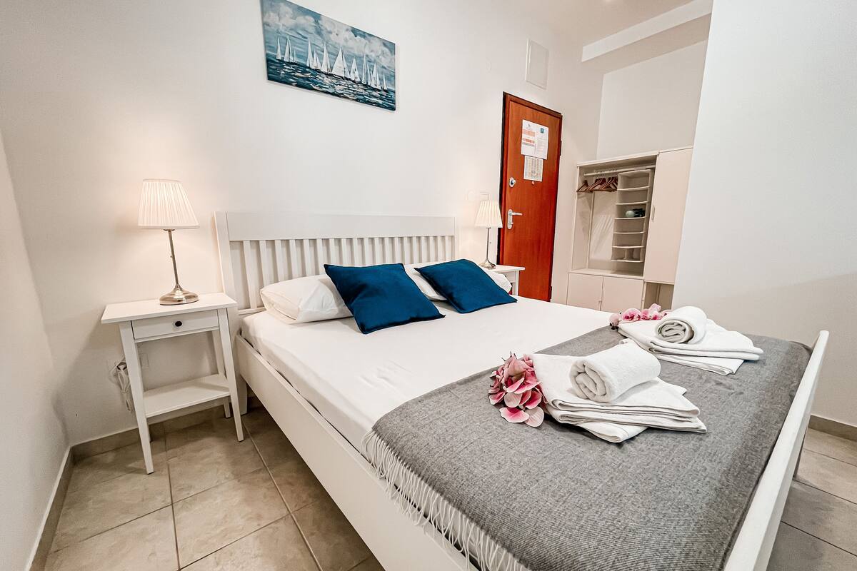Quarto de hotel bem arrumado, com cama, mesa de cabeceira, abajur, porta e espelho.