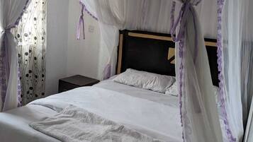 Uma cama com dossel, uma mesa de cabeceira e uma cortina estampada.
