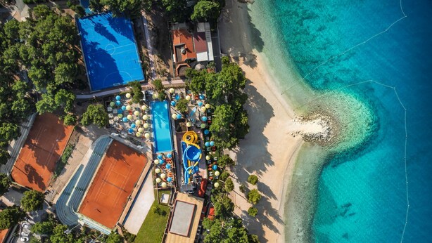 Vista aérea de um resort com praia, quadra de tênis e área de piscina.