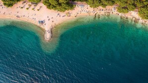 Vista aérea de uma praia com águas turquesa cristalinas, areal e uma fileira de guarda-sóis.