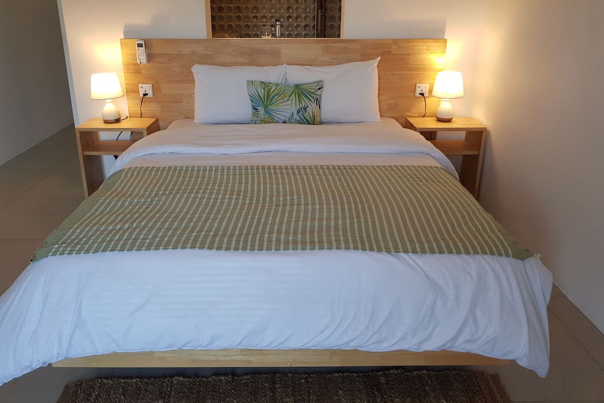 Cama bem arrumada com colcha verde listrada e almofadas brancas, com duas mesas de cabeceira com luminárias de cada lado.