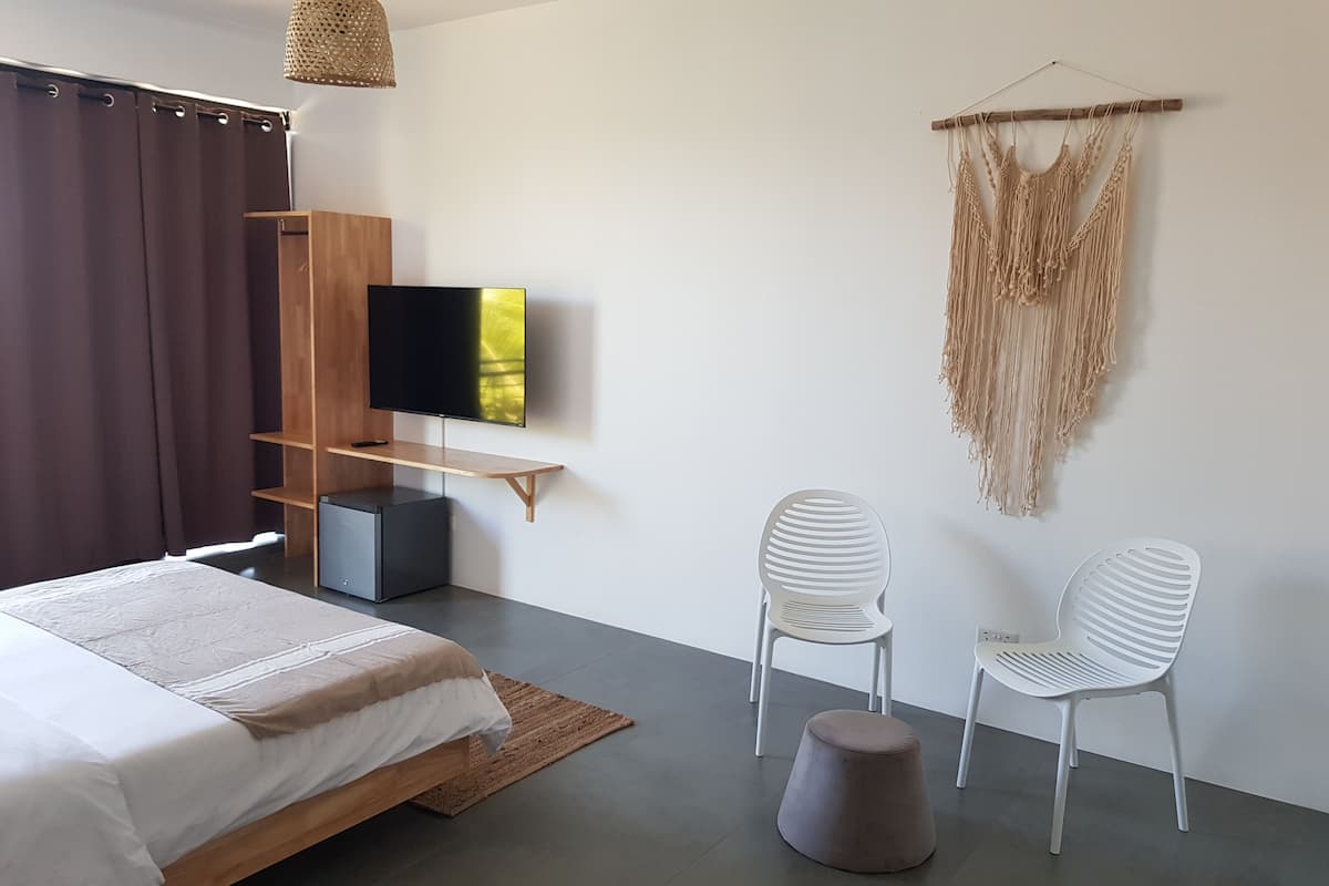 Um quarto moderno com uma cama, uma televisão, duas cadeiras e um painel de parede em macramé.