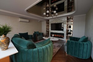 Uma sala de estar moderna com sofás cor turquesa, uma TV de tela plana, uma lareira e um lustre.