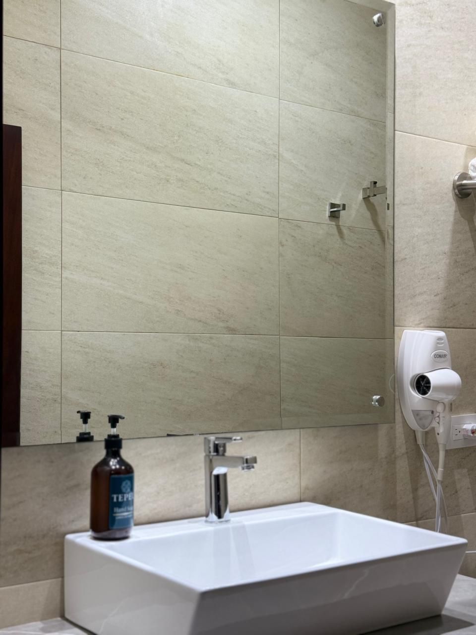 Casa de banho com lavatório branco, espelho e secador de mãos.