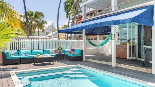 Área de piscina com cerca branca, toldo azul e piscina com escadas.