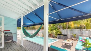 Uma área externa coberta com piscina, rede e um espaço de estar com almofadas.