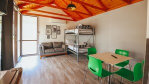 Quarto compacto com uma cama beliche, um sofá, uma mesa com cadeiras e uma janela grande.