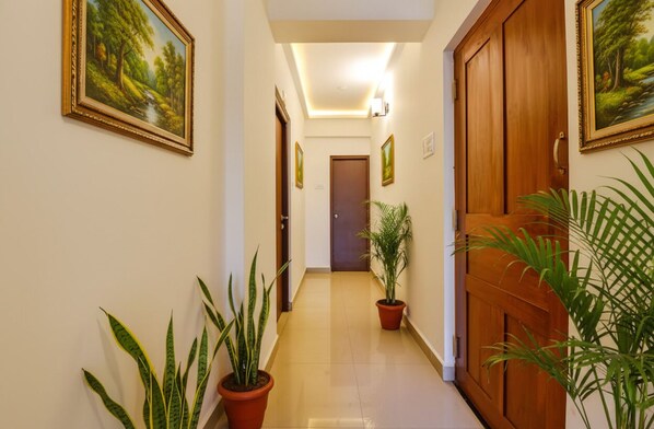 Um corredor com porta de madeira, plantas em vasos e quadros nas paredes.