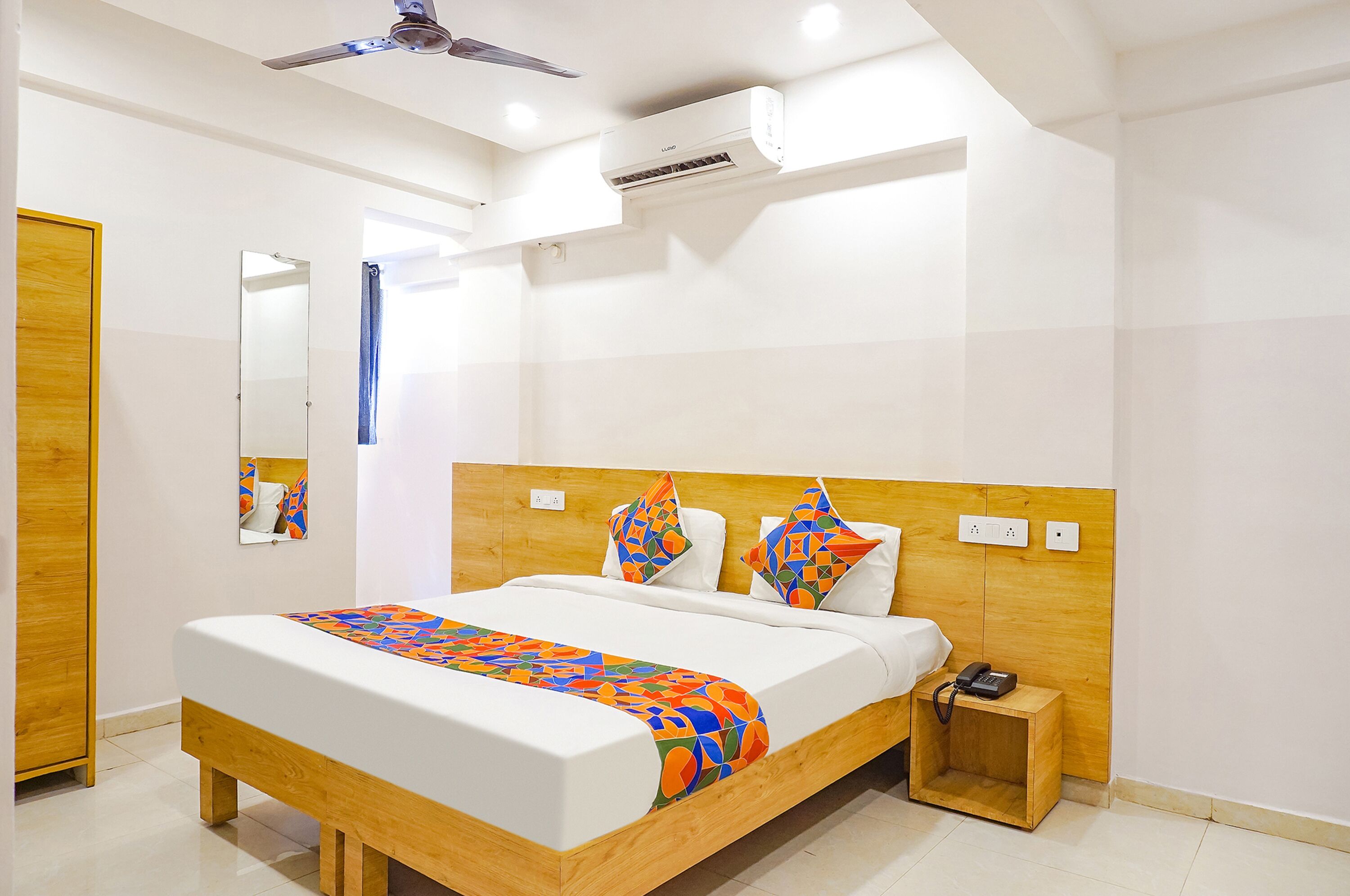 Quarto de hotel moderno com estrutura de cama de madeira, ventoinha no teto, ar condicionado e mesa de cabeceira com telefone.
