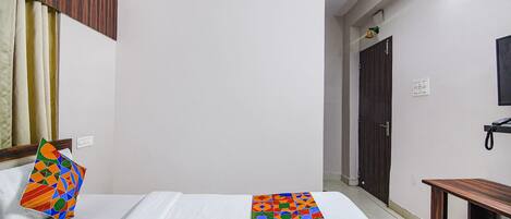 Quarto de hotel com cama, cobre de cama colorido, cabeceira de madeira, mesa de cabeceira e uma porta.