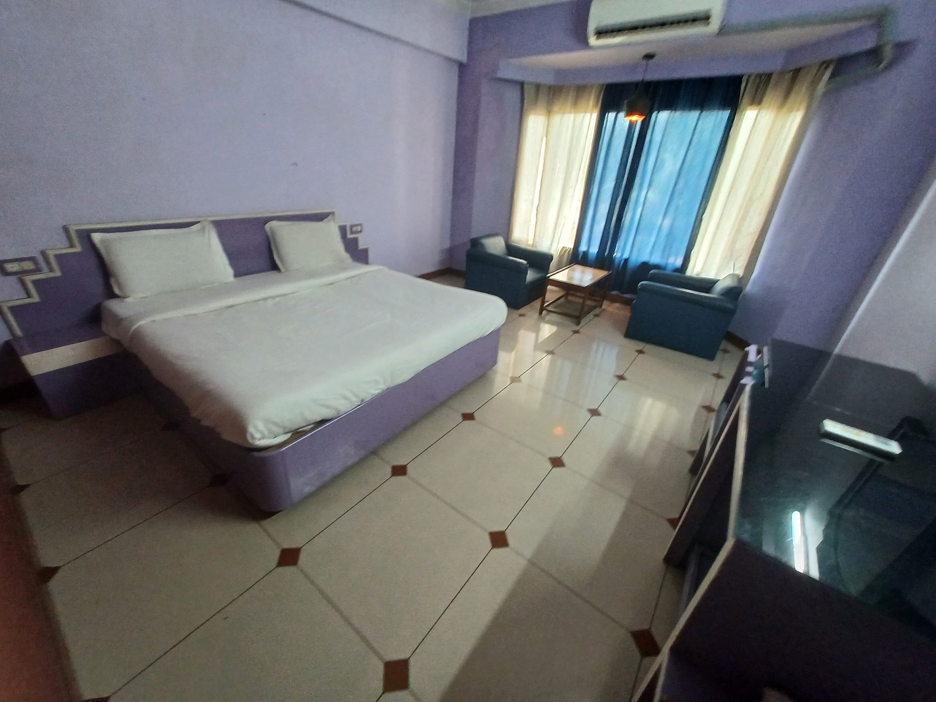 Quarto de hotel com cama, sofá, mesinha e televisão.