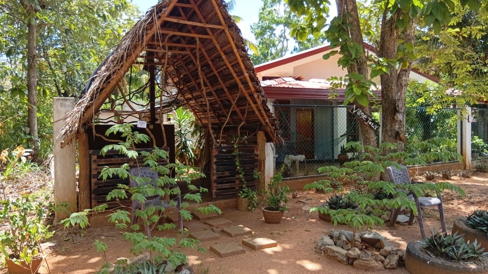 Área externa rústica com estrutura de madeira, plantas em vasos e uma cadeira.