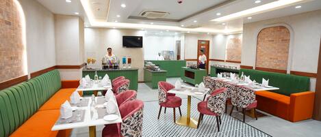 Um restaurante com assentos em estofados verdes, cadeiras vermelhas e piso ladrilhado.