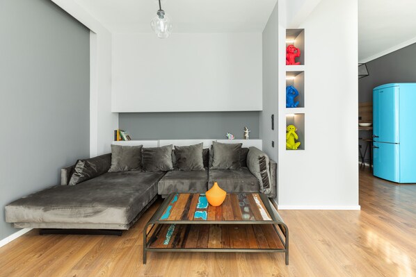 Uma sala de estar moderna com um sofá seccional, uma mesa de centro com tampo de madeira e uma geladeira azul ao fundo.