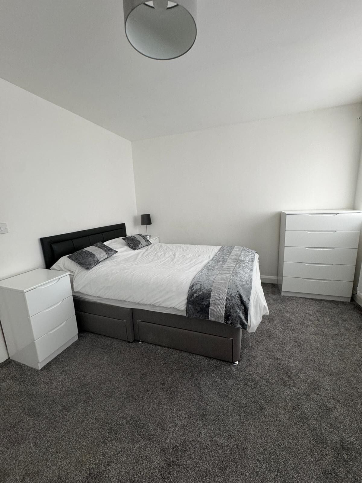 Um quarto com cama, mesas de cabeceira e cómoda.