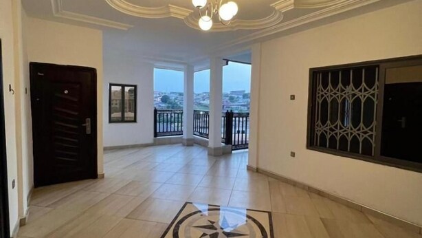 Interior espaçoso com teto alto, lustre central, piso estampado e vista através de uma porta de vidro.
