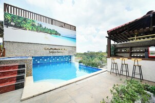 Área da piscina com placa para o Hotel California Sagong Serenity, um bar com banquetas e uma parede de pedra.