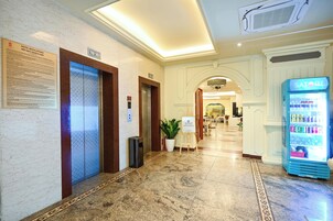Um saguão de hotel com piso de mármore, uma máquina de venda automática Sator! e um aviso sobre regulamentos do hotel.