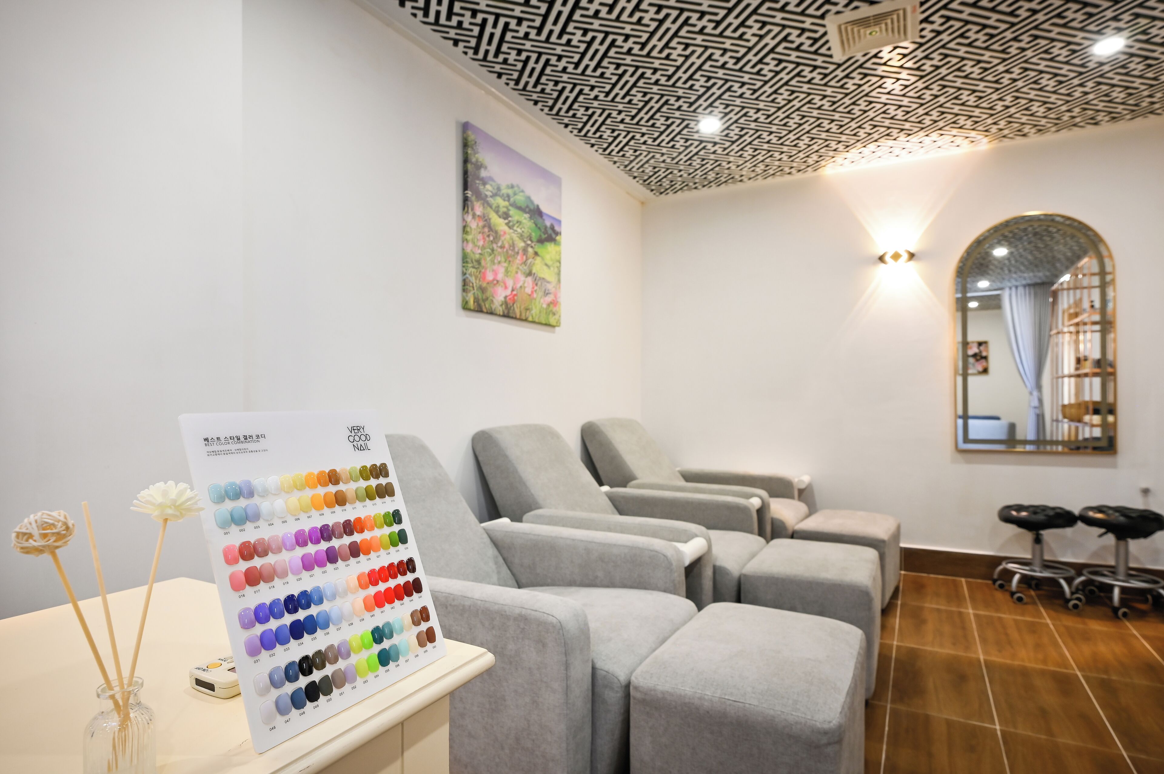 Um quarto com cadeiras estofadas cinzentas, um diagrama de paleta de cores, um espelho e um teto com padrão geométrico.
