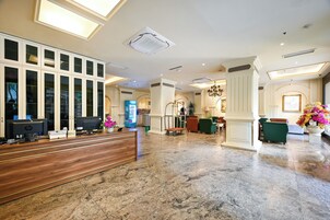 Um saguão de hotel com balcão de recepção, computadores, máquina de venda automática e áreas de estar.