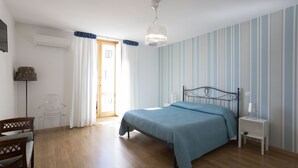 Quarto com cama, mesa de cabeceira, luminária, cadeira e janela com cortinas.