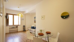 Uma área de refeições com mesa de vidro, cadeiras brancas e um sofá branco ao fundo.