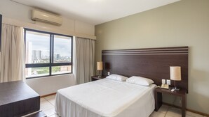 Quarto de hotel com uma cama grande, duas mesas de cabeceira com abajures, uma escrivaninha e uma janela com cortinas.
